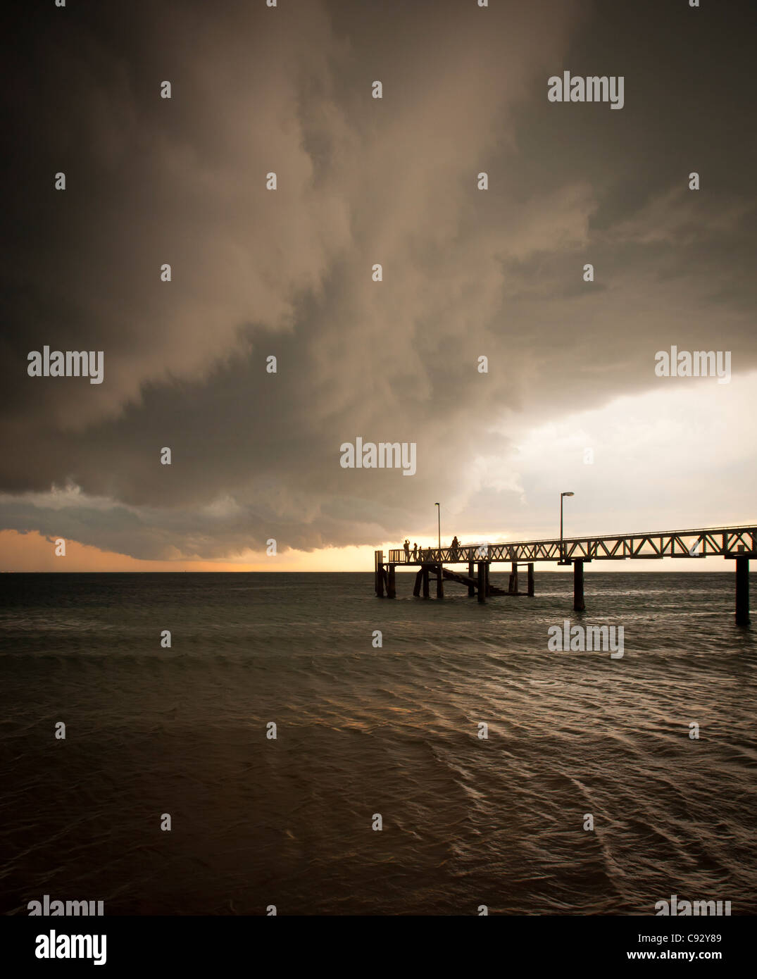 Huge black storm clouds gather as silhouetted people fish off a pier ...