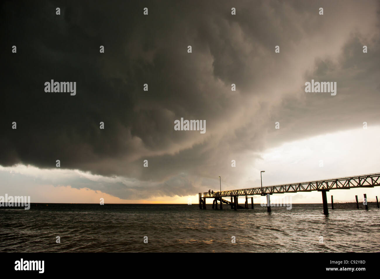 Huge black storm clouds gather as silhouetted people fish off a pier ...