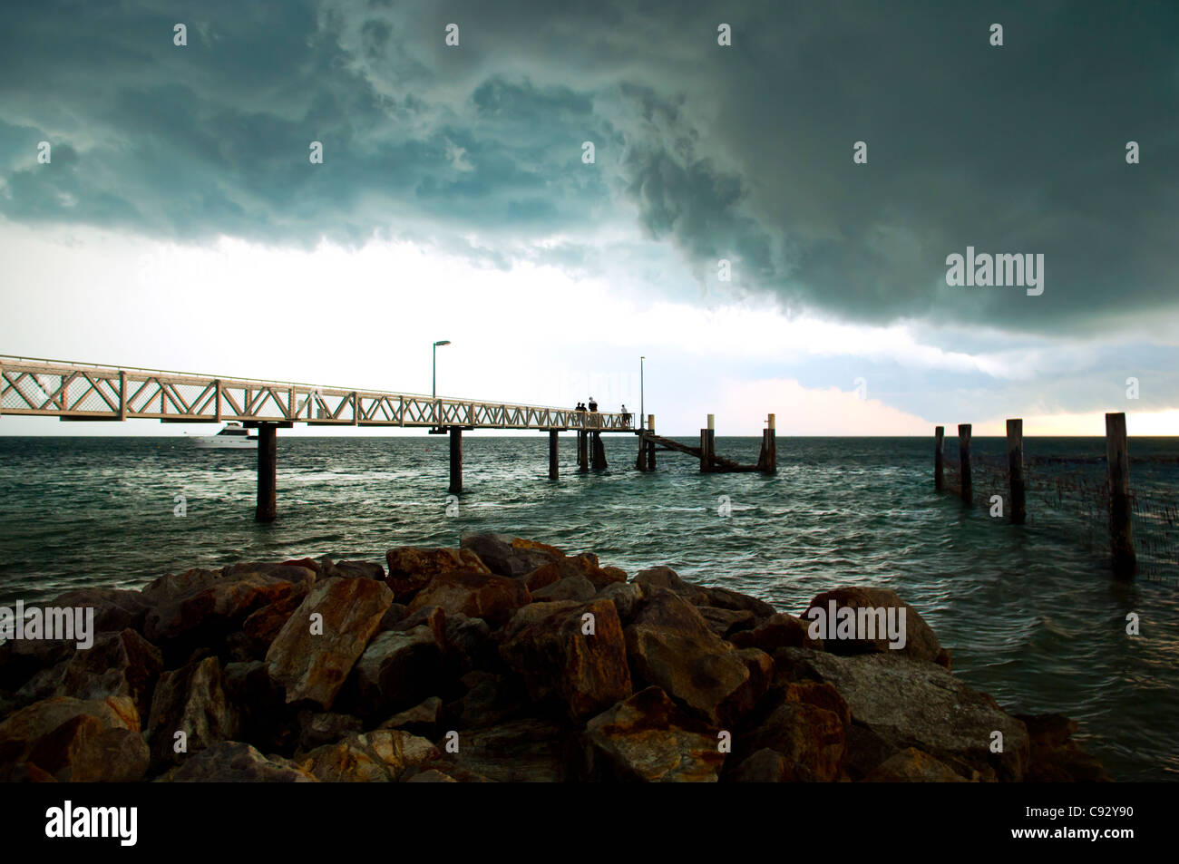 Huge black storm clouds gather as silhouetted people fish off a pier ...
