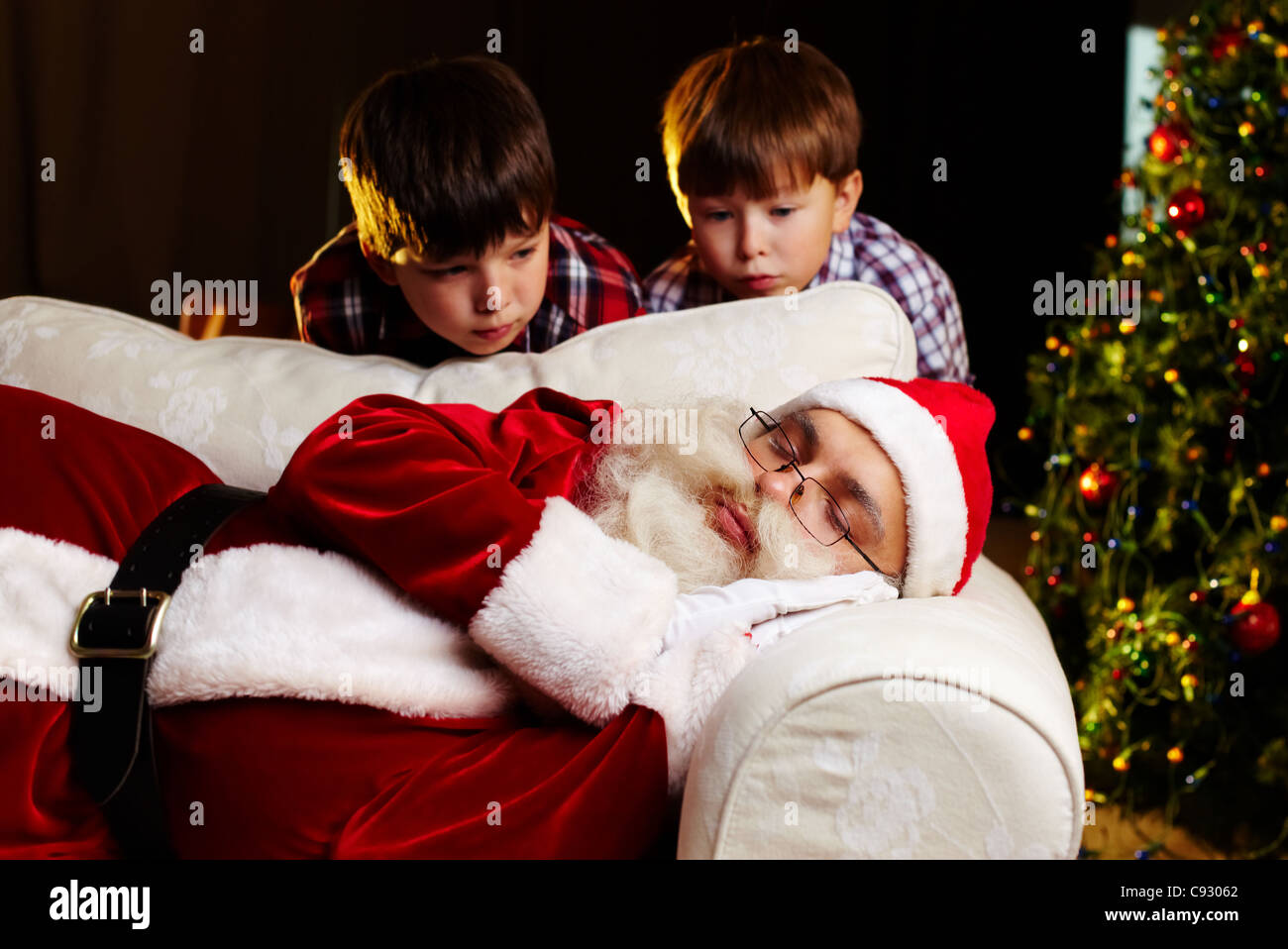 Photo of Santa Claus sleeping on sofa with two amazed kids looking at ...