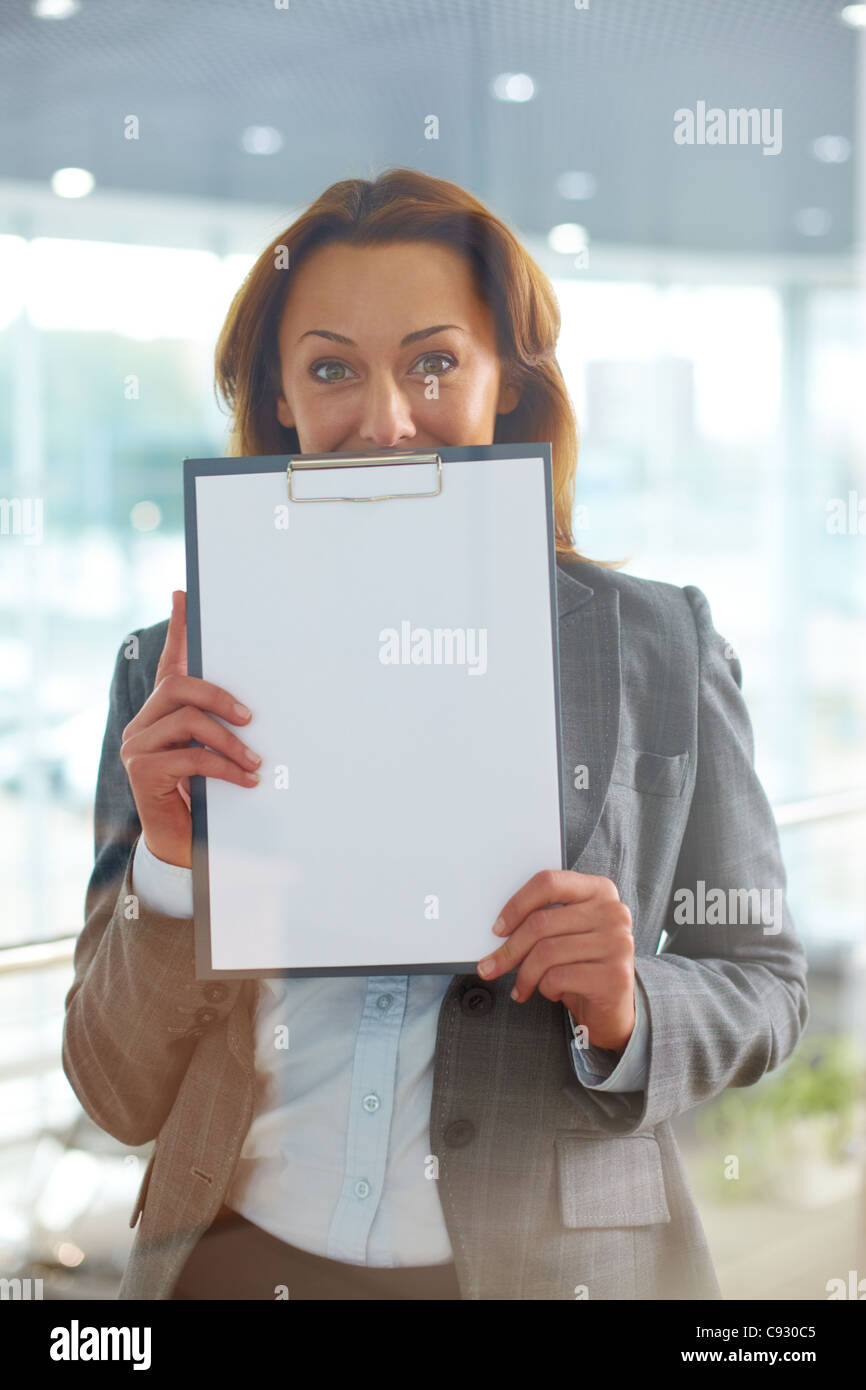 Portrait of businesswoman holding clipboard by her and looking at ...