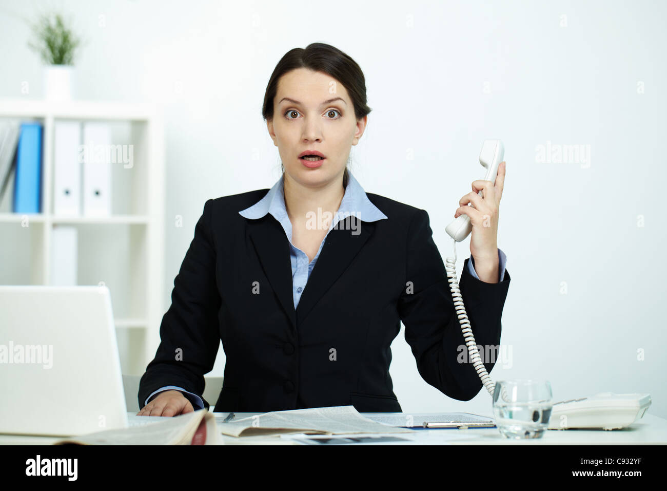 Portrait of amazed office worker with phone receiver looking at camera ...