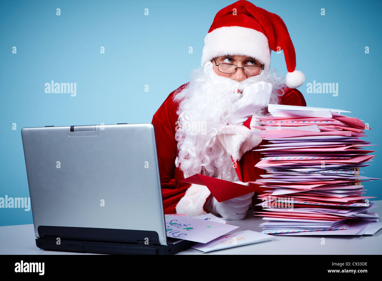 Portrait of pensive Santa Claus in front of laptop and heap of ...