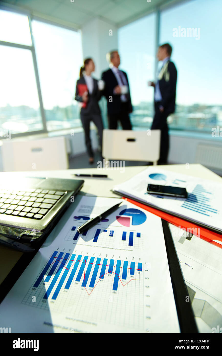 Image of business documents on workplace with three partners on ...