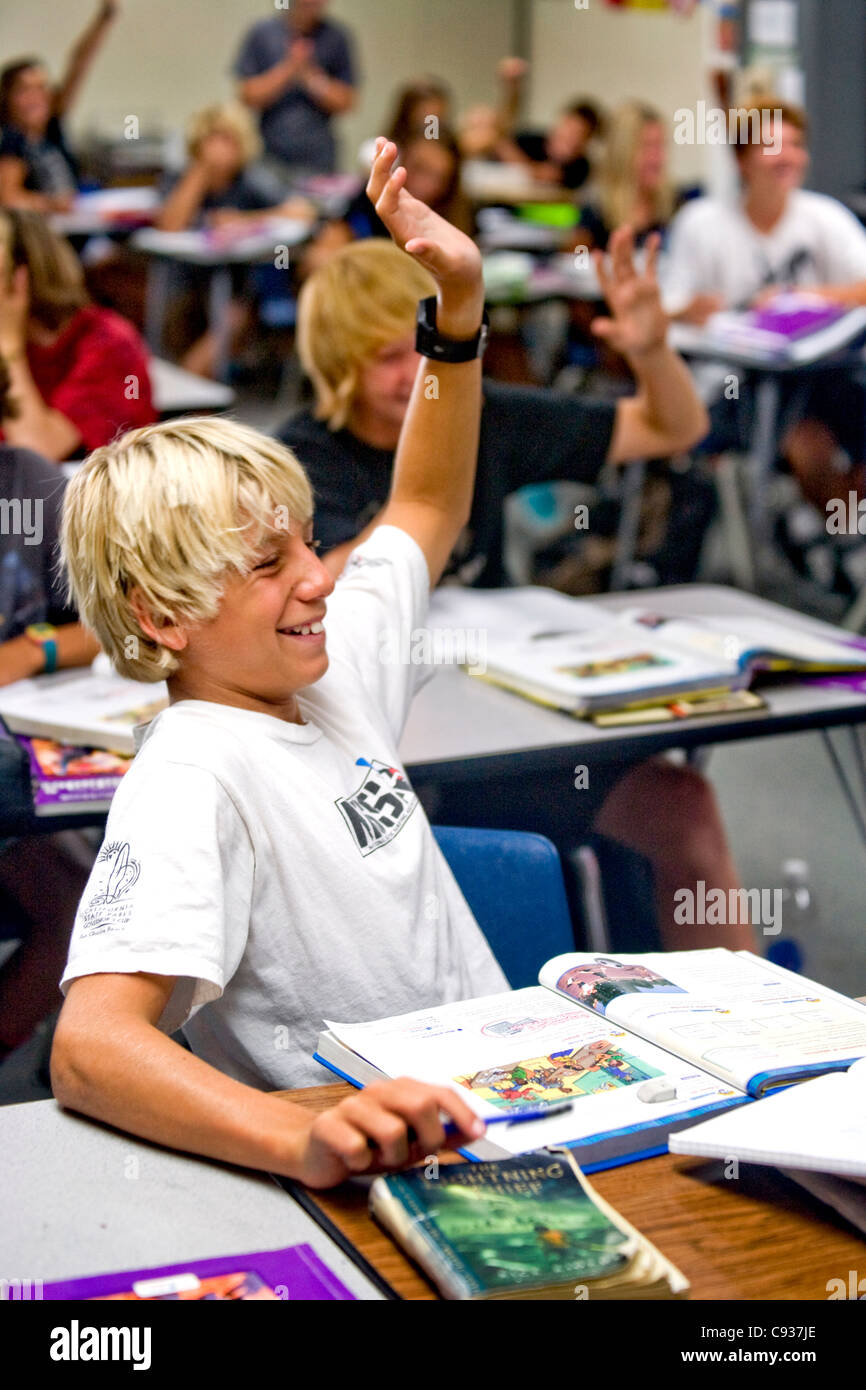 A blonde, enthusiastic eight-grade boy holds up his hand to answer a ...