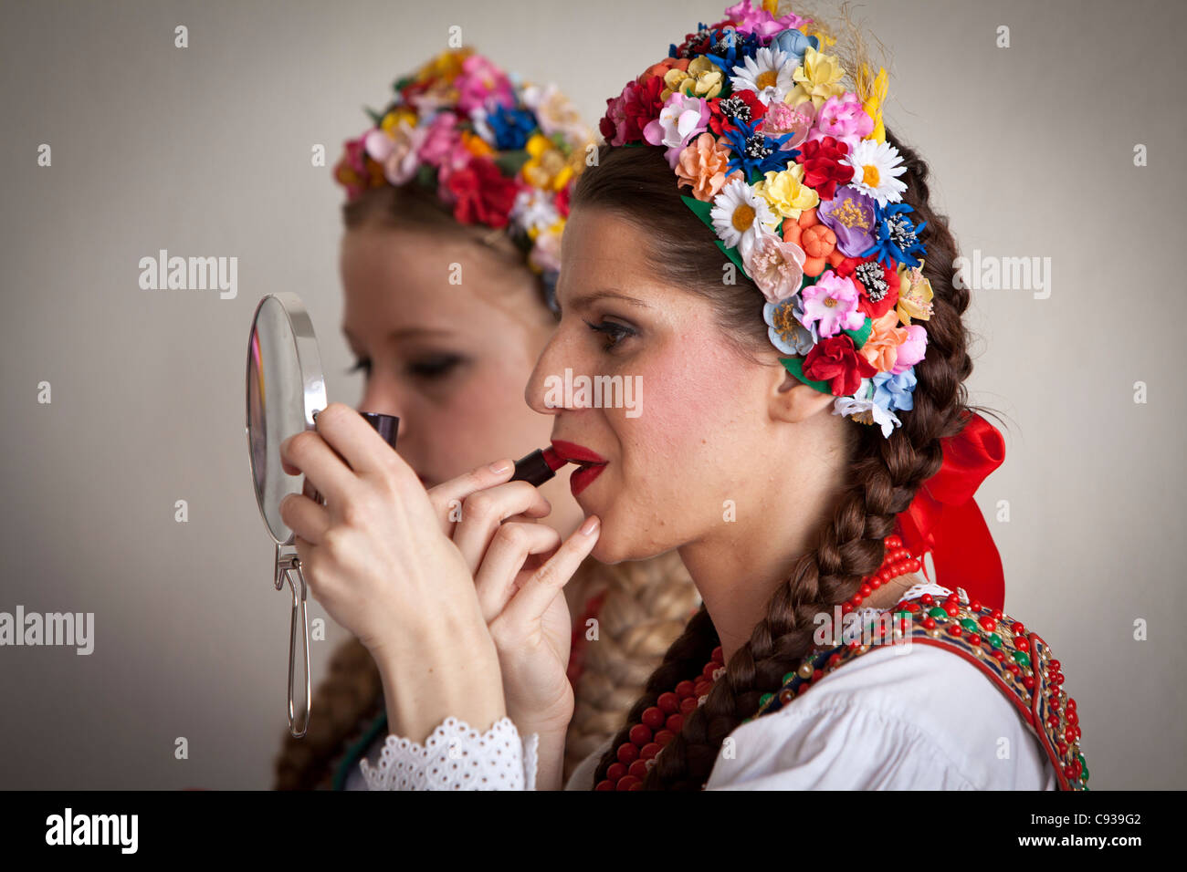 Poland, Cracow. Polish girl in traditional dress applying lipstick ...