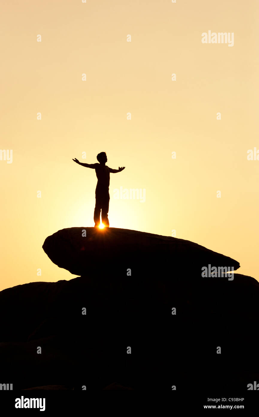 Indian man standing on a rock embracing the sun. Silhouette. India ...