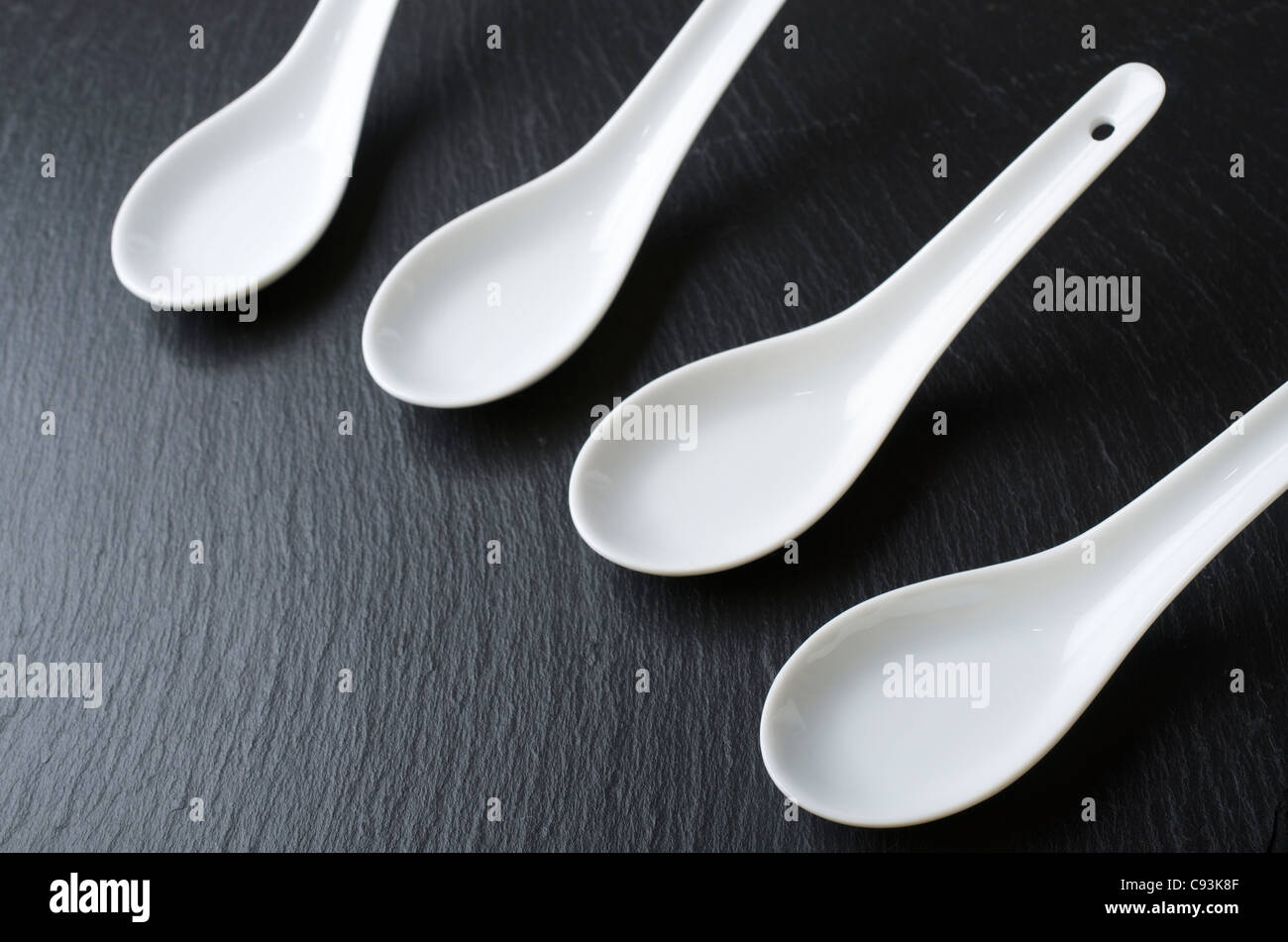 four small white spoons on a table slate Stock Photo - Alamy