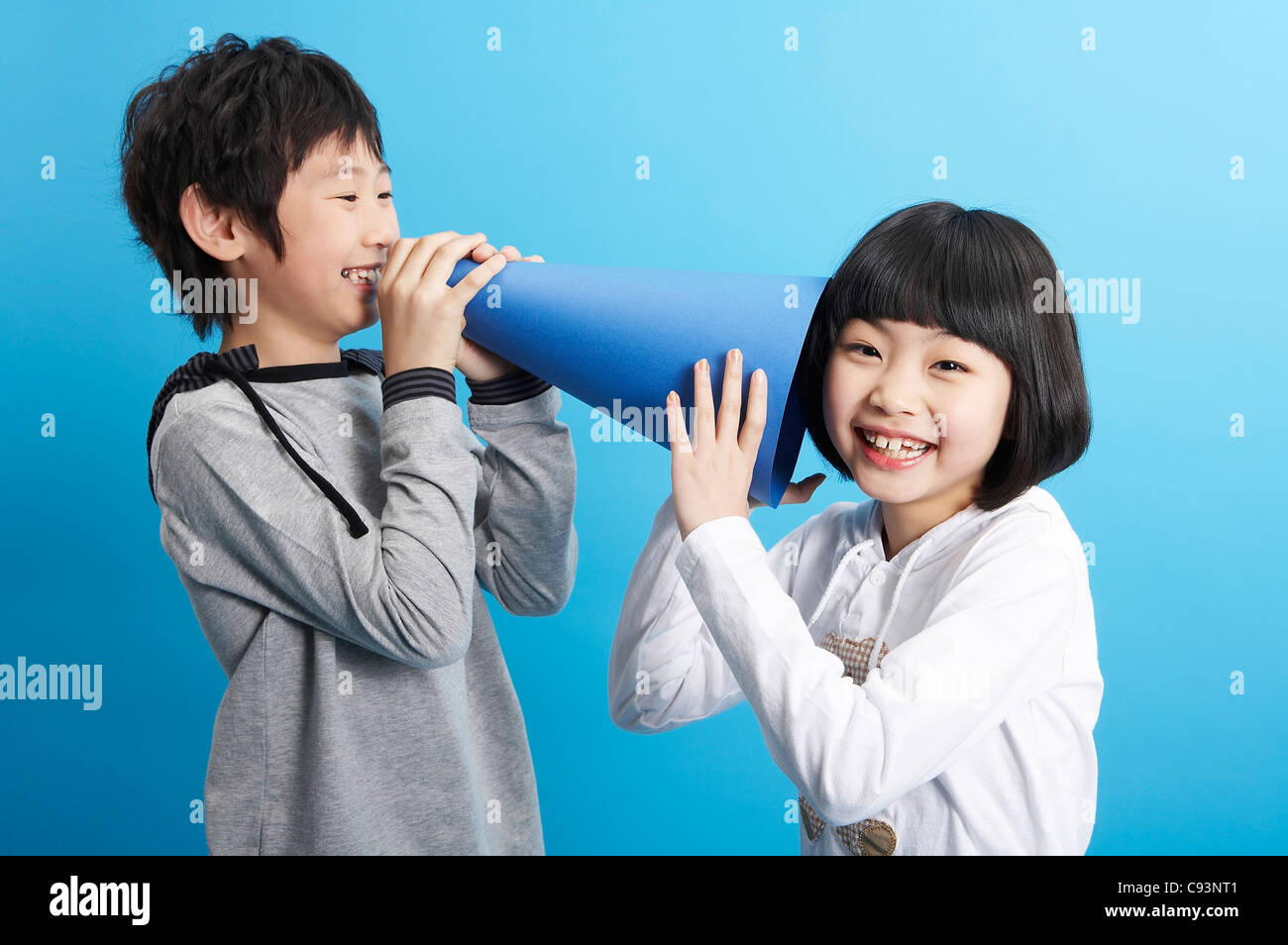 Young boy talking in girls ear with paper megaphone Stock Photo - Alamy