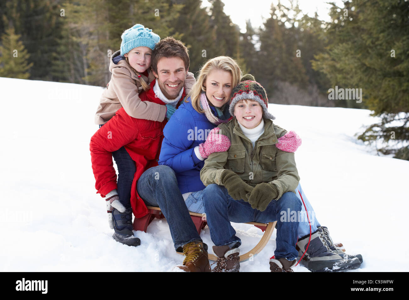 Young Family Sitting On A Sled In The Snow Stock Photo - Alamy