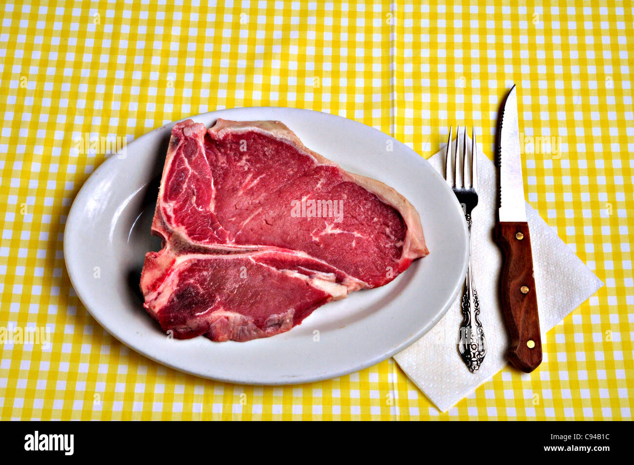 A raw uncooked t-bone steak is laying on a white plate on a white and ...