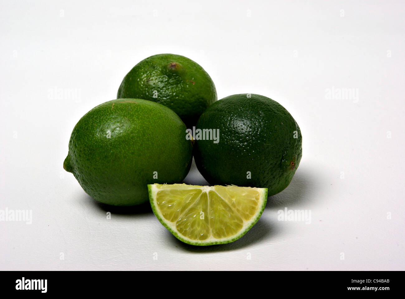 Three whole limes and a slice of lime sits on a white background Stock ...