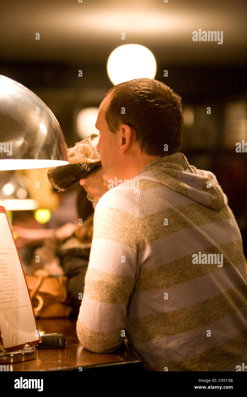 A young man drinking Guinness beer in pub leaning on bar Stock Photo ...