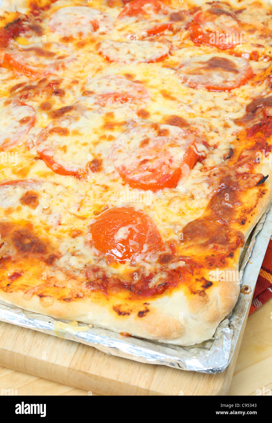 A Sicilian rectangular pizza with cheese and tomato topping on a baking ...