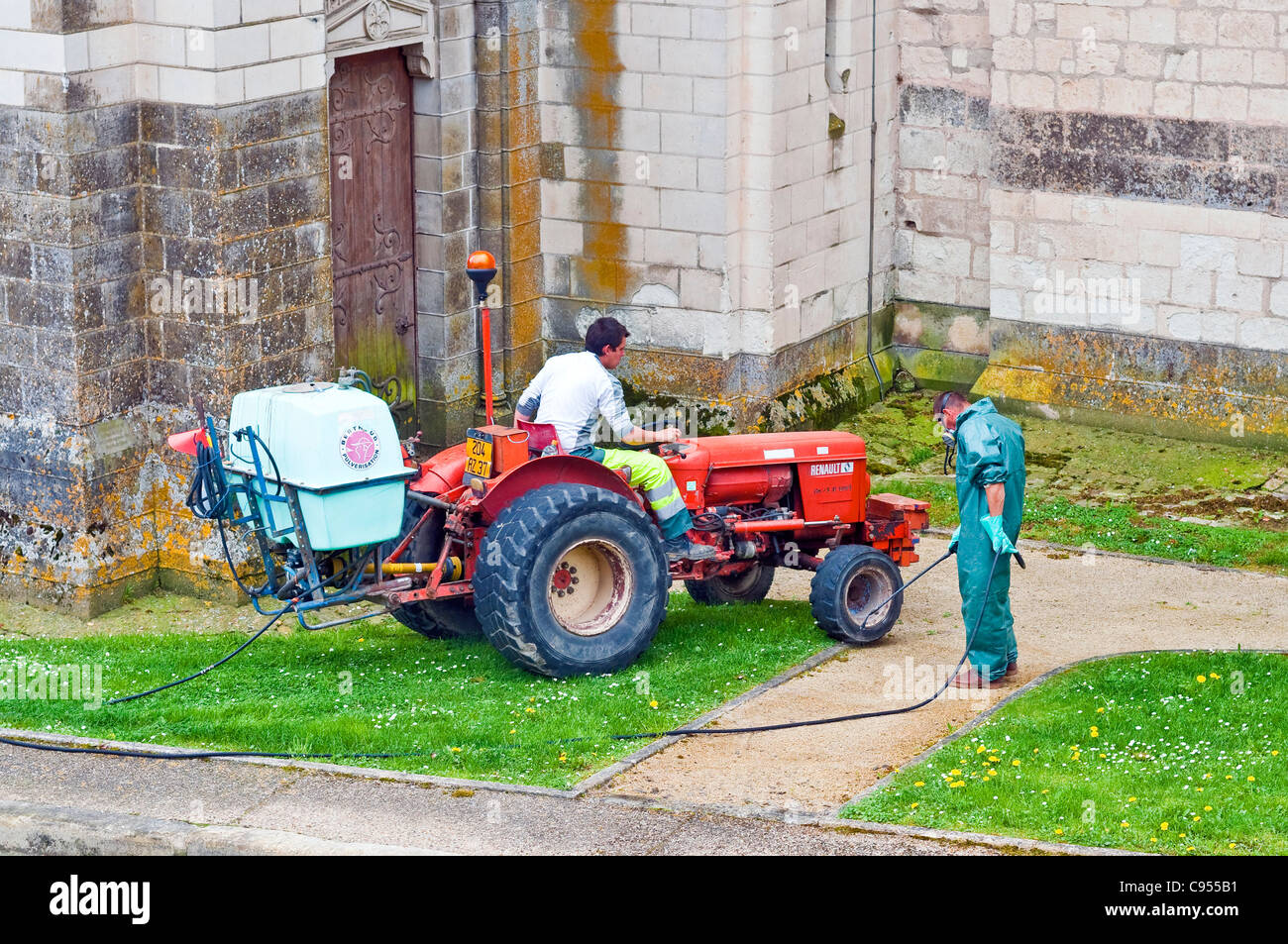 Tractor and worker in protective overalls and mask spraying weeds ...