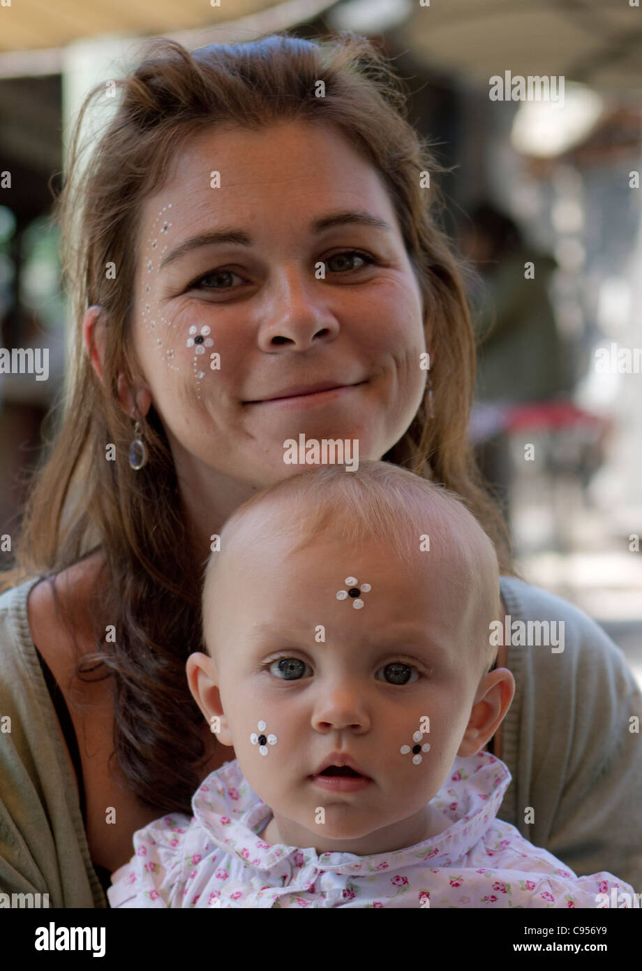 Mother and baby, both with matching flowers painted on their faces ...