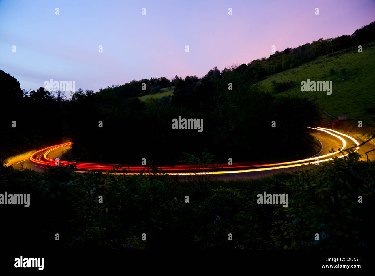 A tight bend on a road with car light trails at dusk in the Surrey ...