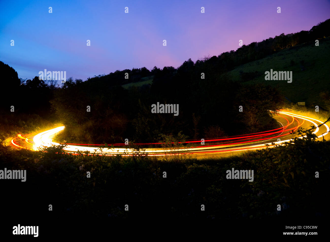 A tight bend on a road with car light trails at dusk in the Surrey ...