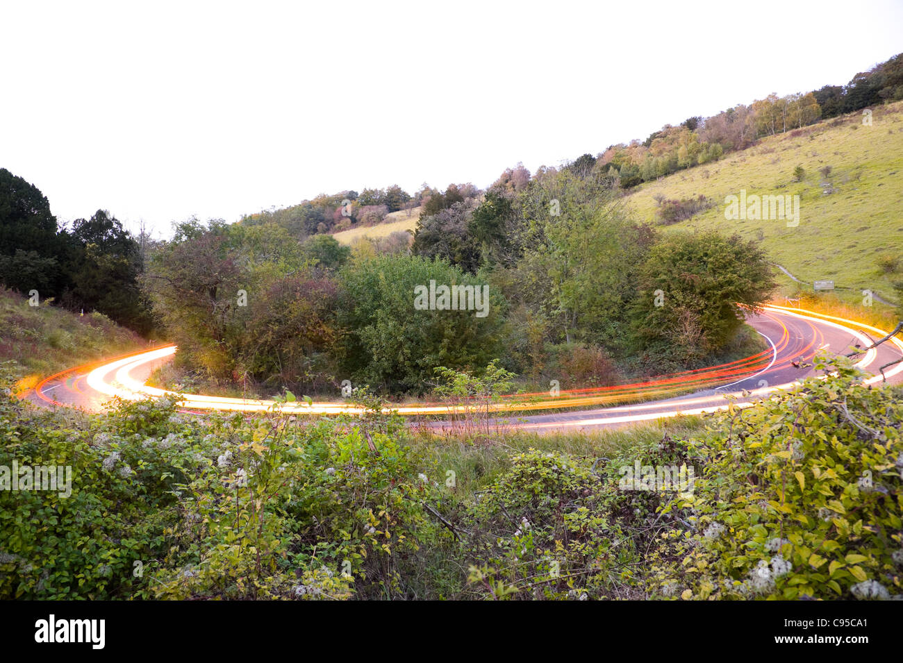 A tight bend on a road with car light trails at dusk in the Surrey ...