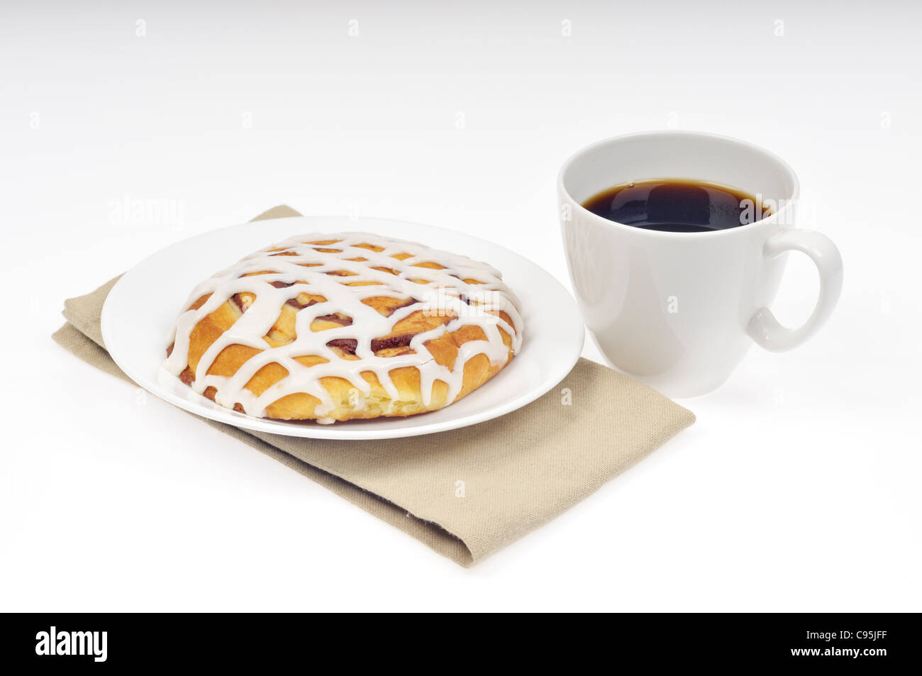 Iced danish pastry on white plate with cloth napkin and cup of black ...