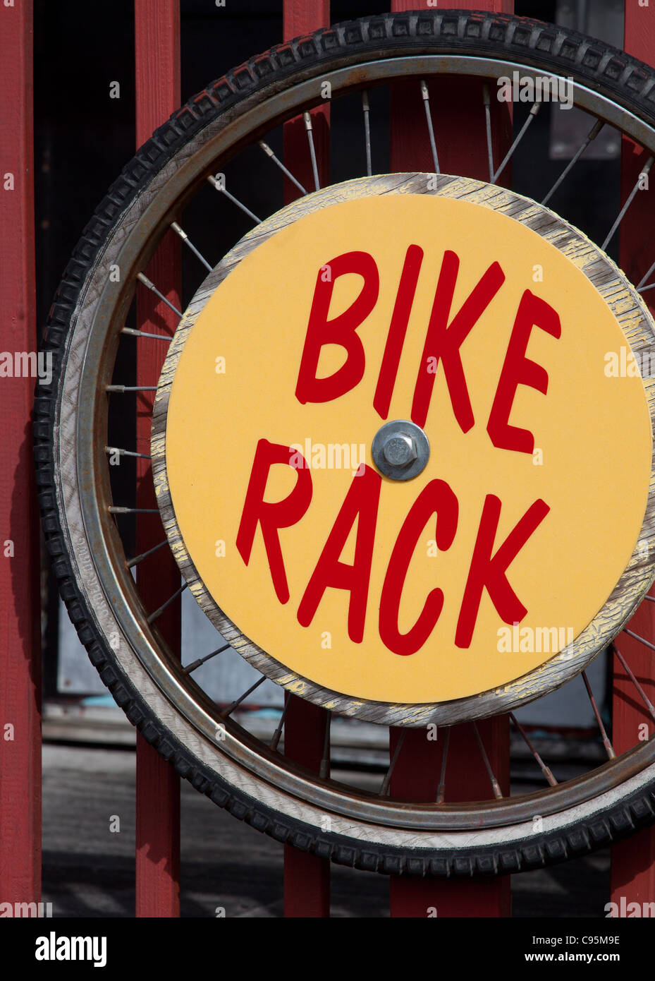 A bright red and yellow bike rack sign mounted on a red fence Stock ...