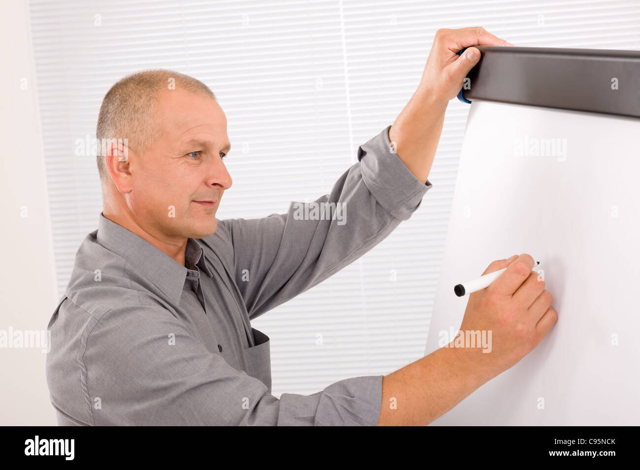 Handsome mature businessman writing at empty flip chart looking aside ...