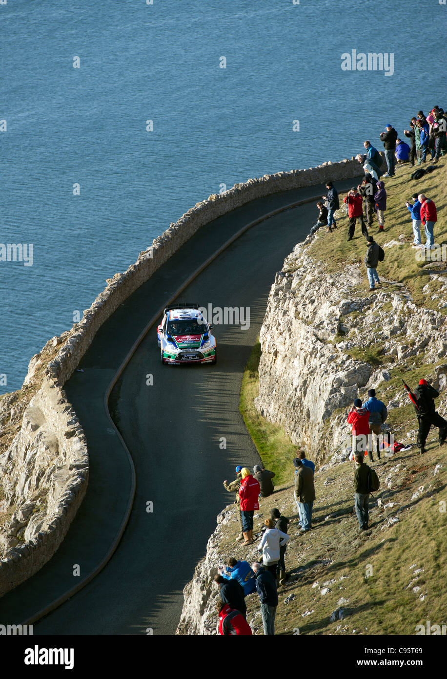 People watch from the hillside as a rally car rounds a corner during a ...