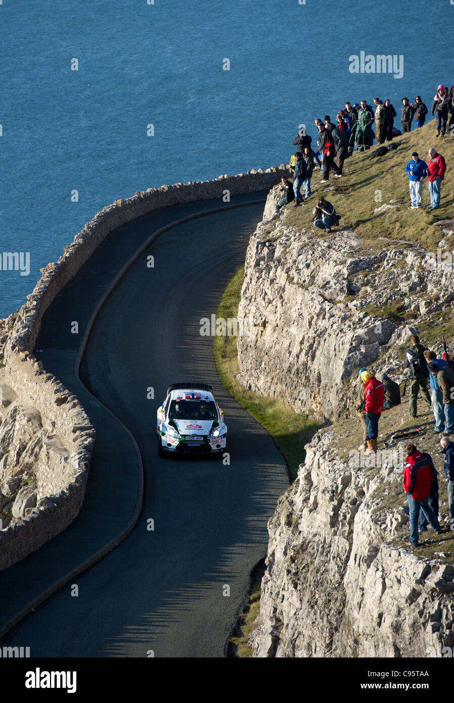 People watch from the hillside as a rally car rounds a corner during a ...