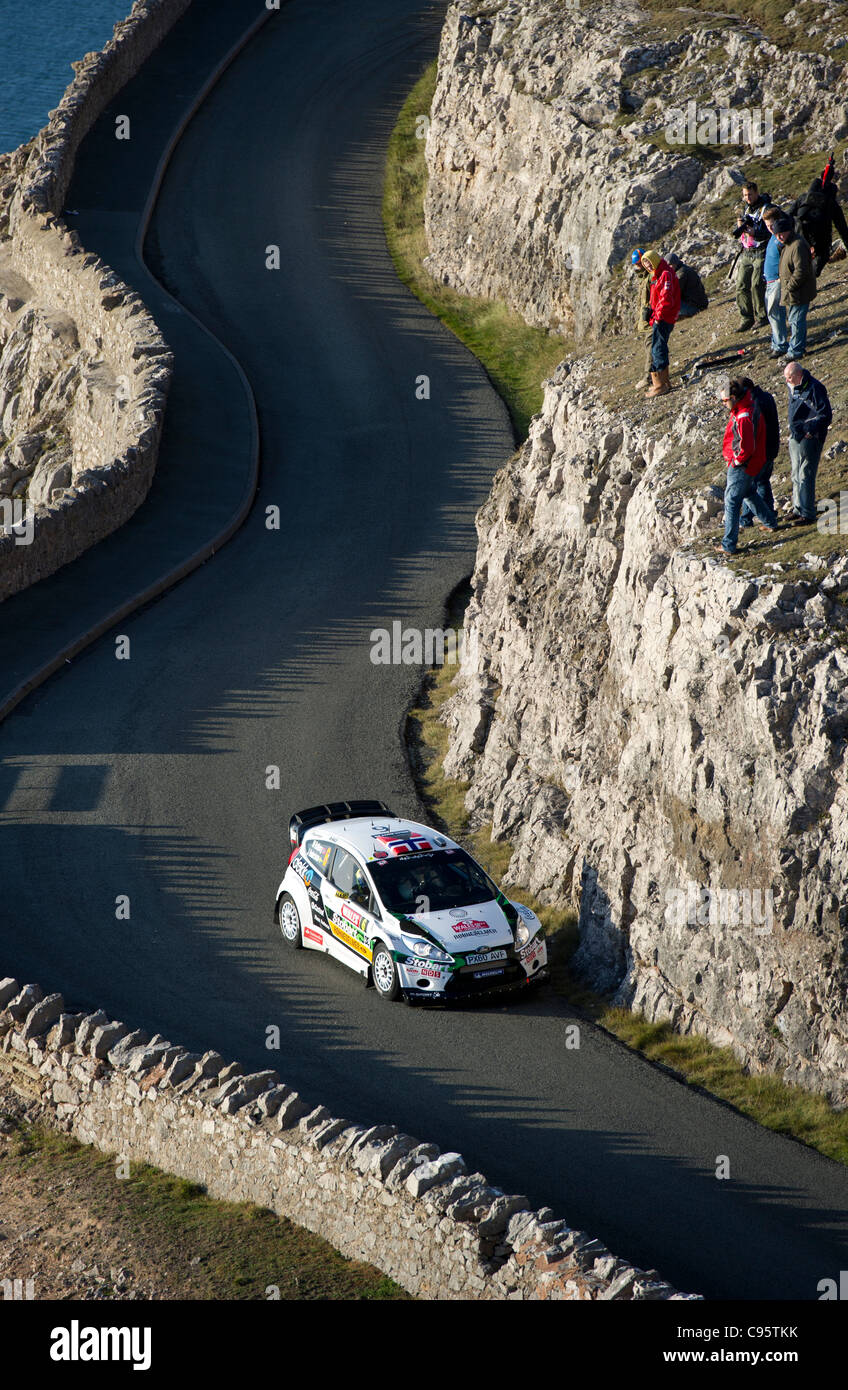People watch from the hillside as a rally car rounds a corner during a ...