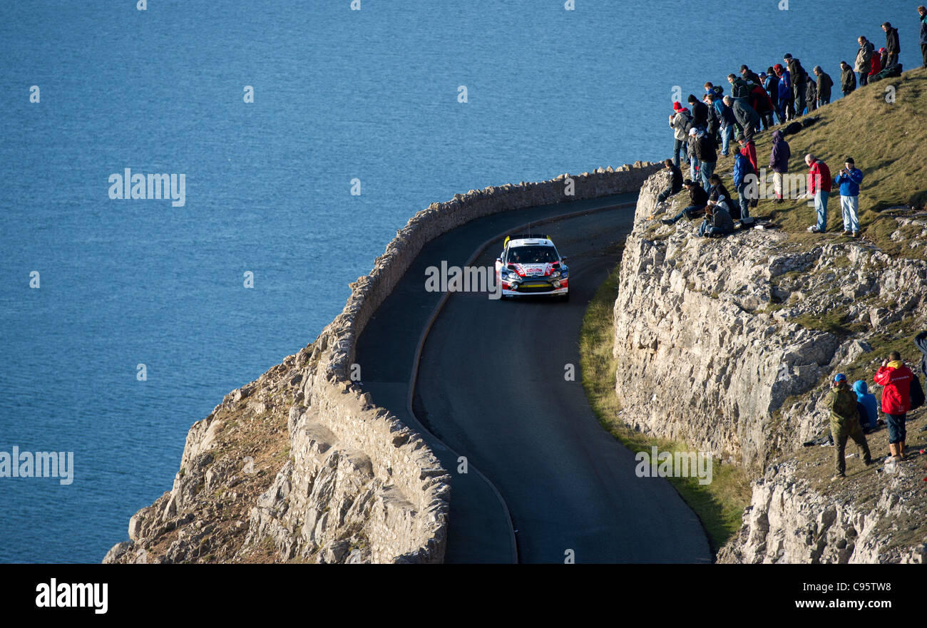 People watch from the hillside as a rally car rounds a corner during a ...
