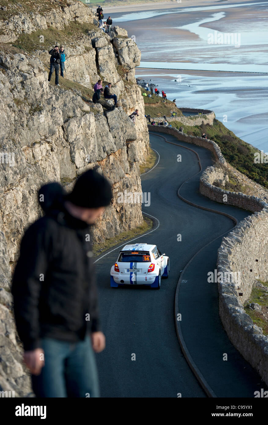 People watch from the hillside as a rally car rounds a corner during a ...