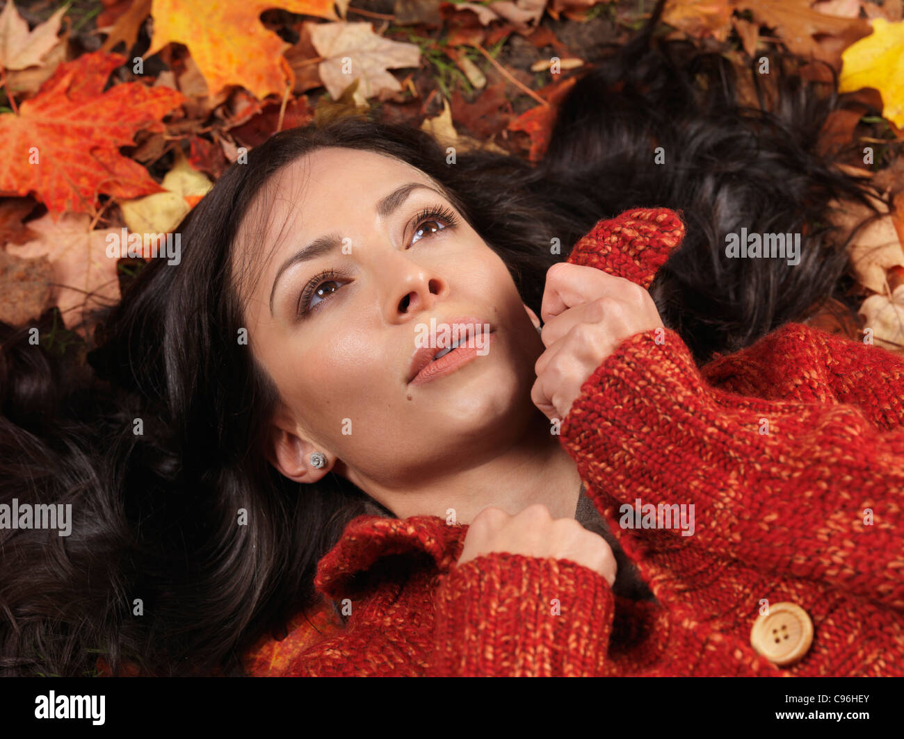 Beautiful woman with dreamy expression lying on colorful fallen leaves ...