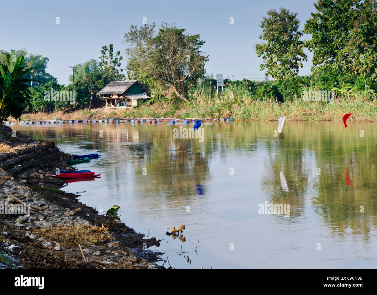 Two small boats colored solid red and solid blue on river shore with 3 ...