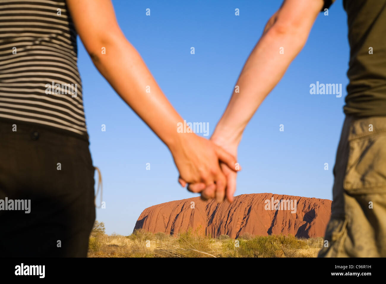 Couple holding hands with Uluru (Ayers Rock) in background. Uluru-Kata ...