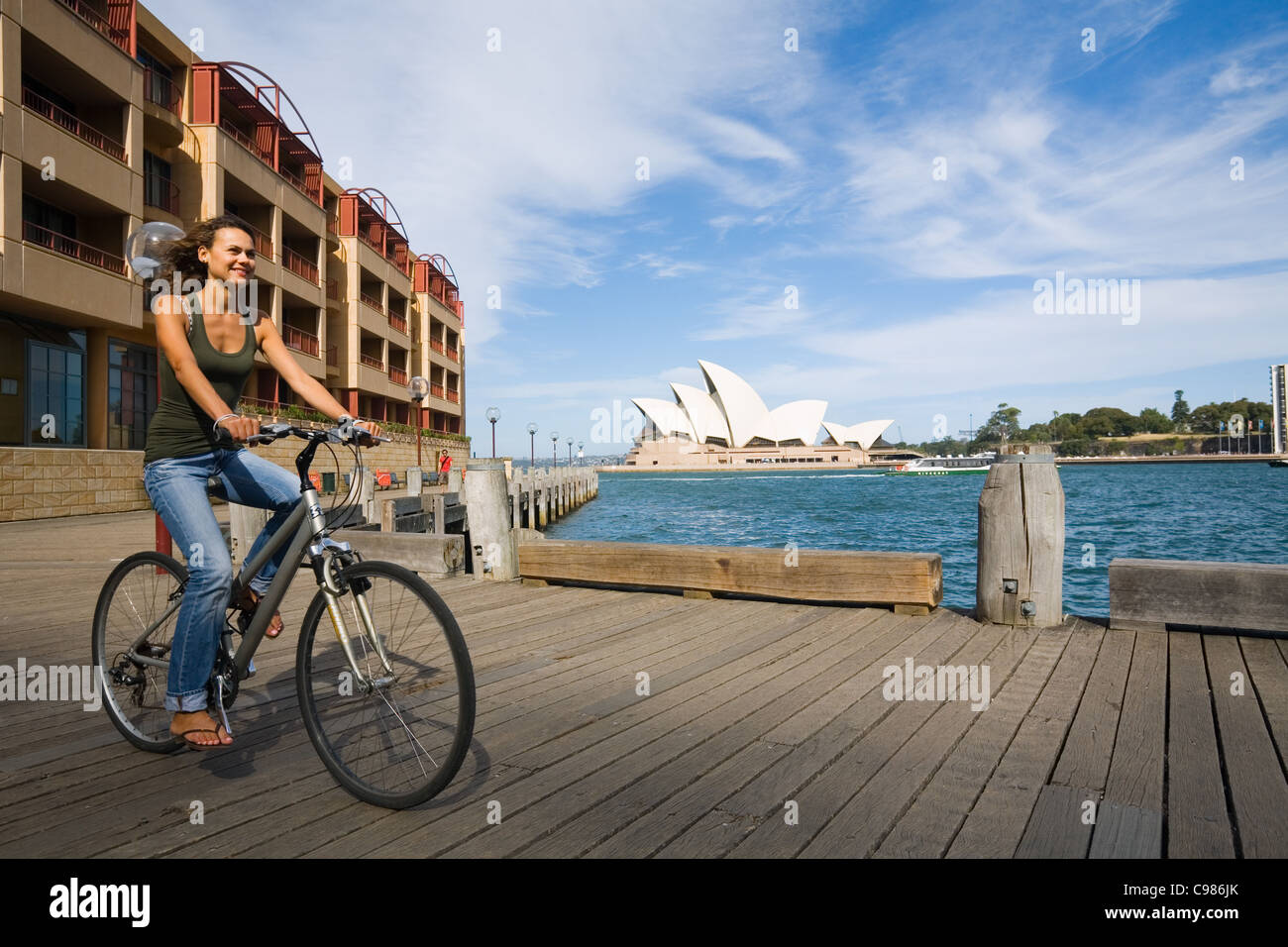 Woman riding bicycle along Sydney harbour with the Opera House in ...