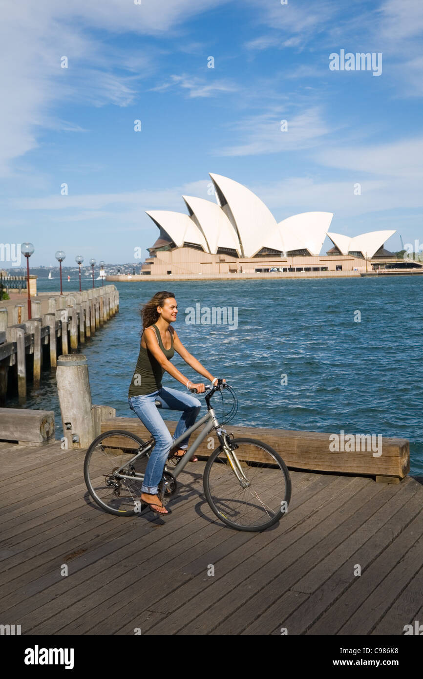 Woman riding bicycle along Sydney harbour with the Opera House in ...