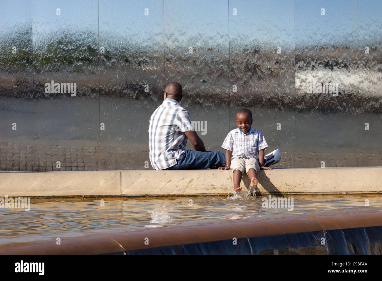 A n afro caribbean father and son sitting by the water on the concourse ...