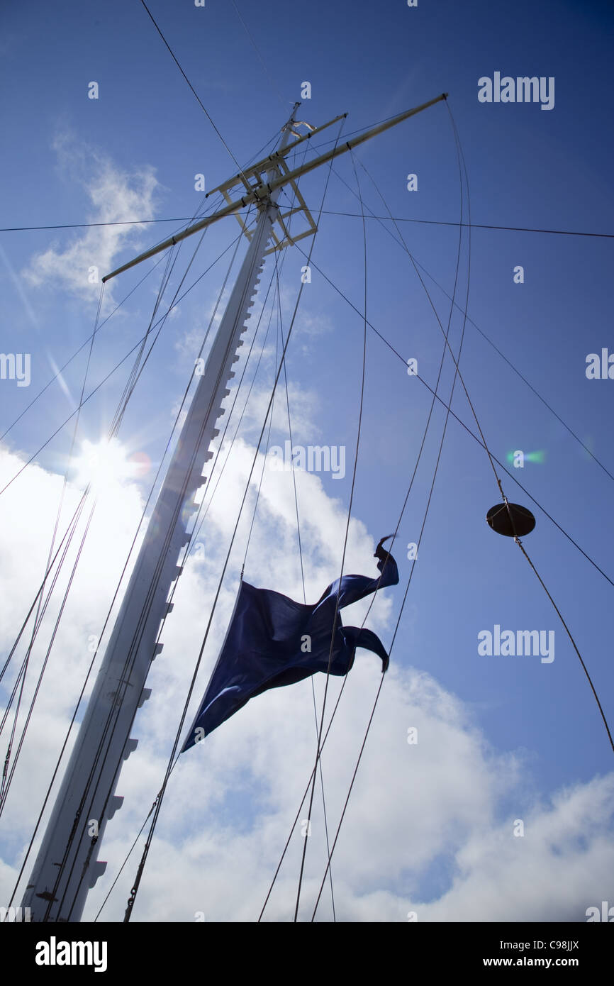A Colour photo of a ships mast and a blue flag being raised. Set ...