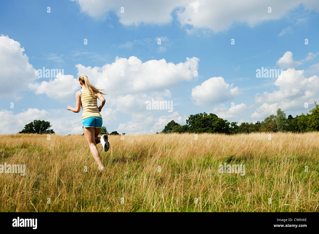 Young woman jogging through field on sunny day Stock Photo - Alamy