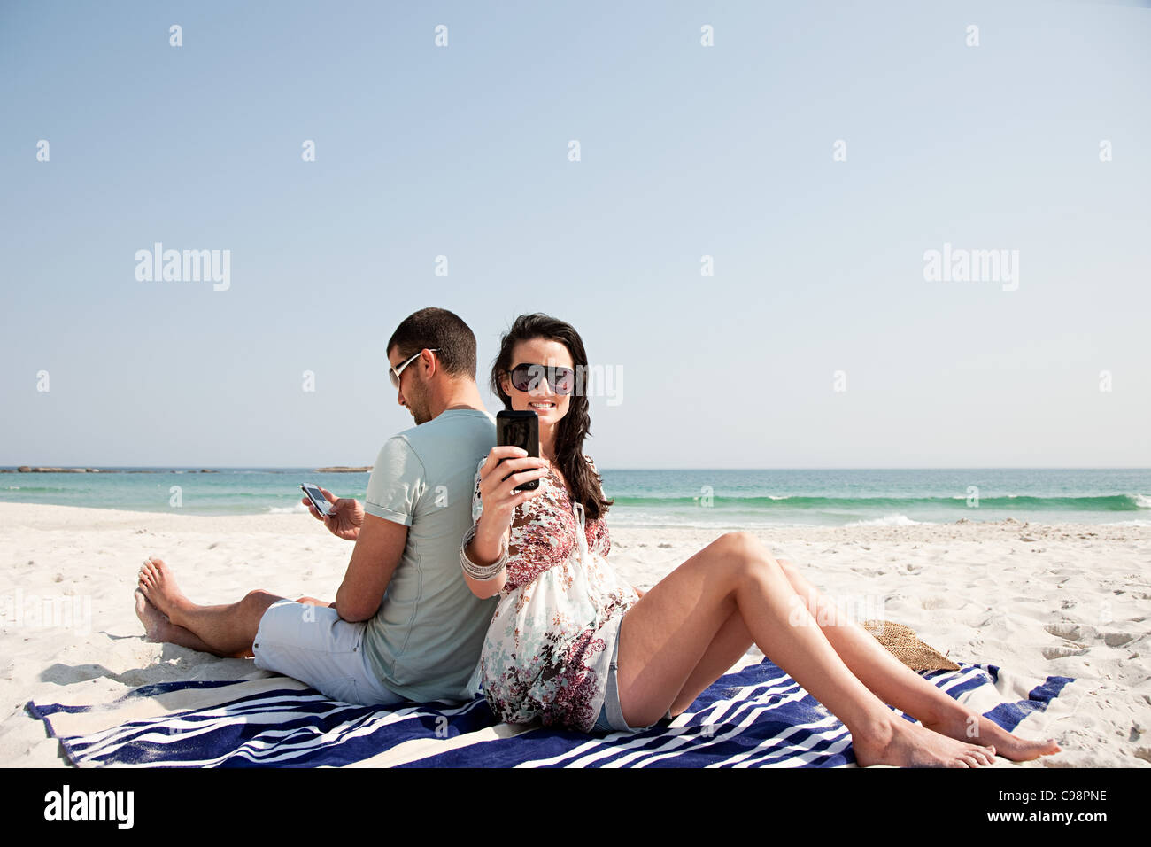 Couple Sunbathing On Beach Looking At Their Mobile Phones Hi Res Stock
