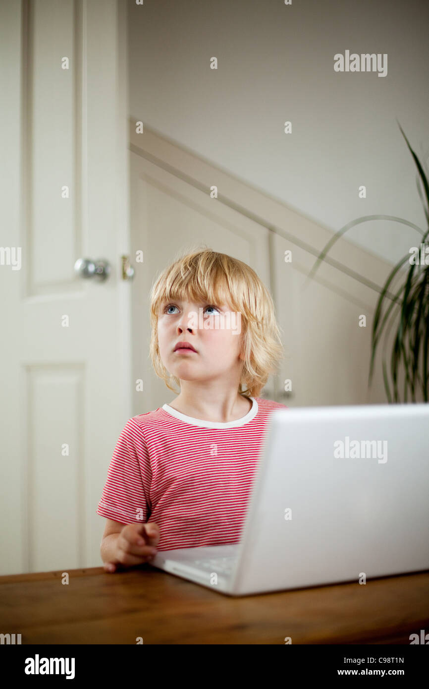 Boy looking up from laptop on desk Stock Photo - Alamy