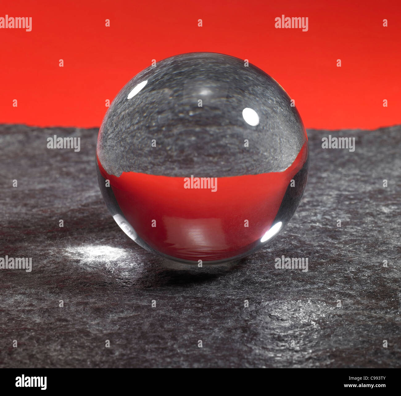 a clear crystal ball on rough dark grey stone surface in front of red ...