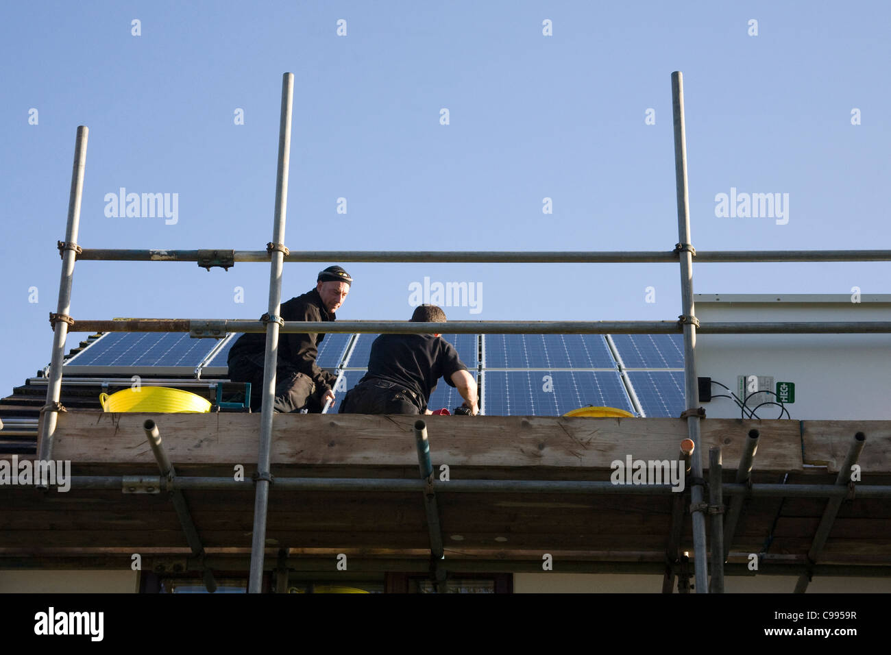UK Two men standing on scaffolding fitting solar panels on a domestic ...
