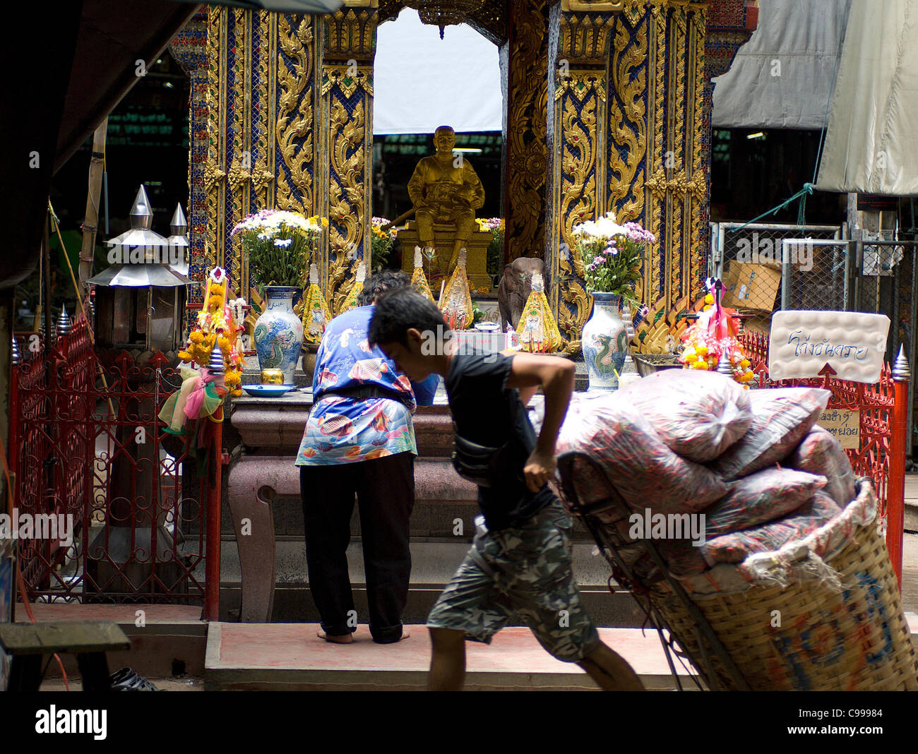 A porter pulls a heavily laden trolley past a devotee at a shrine in ...