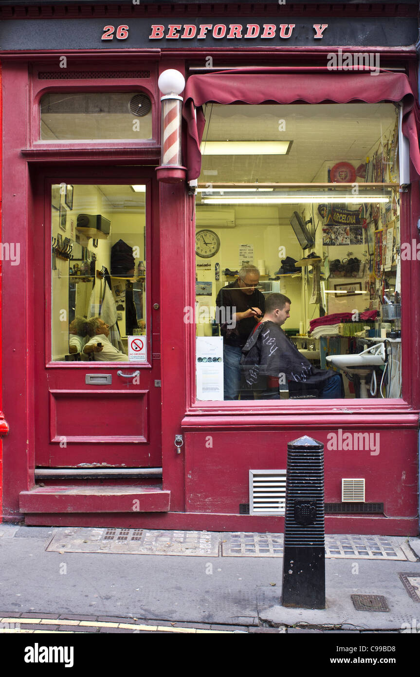 A man has his hair cut in front of the window in a traditional barbers ...