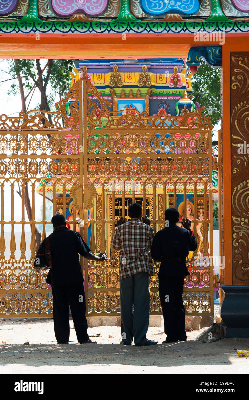 Three indian men standing outside the gates of a village hindu temple ...