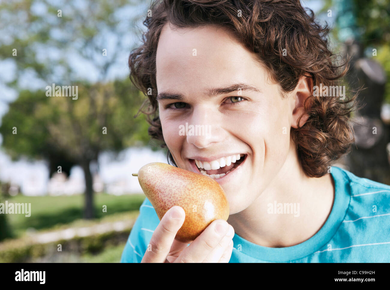 Italy, Tuscany, Magliano, Close up of young man eating pear, smiling ...