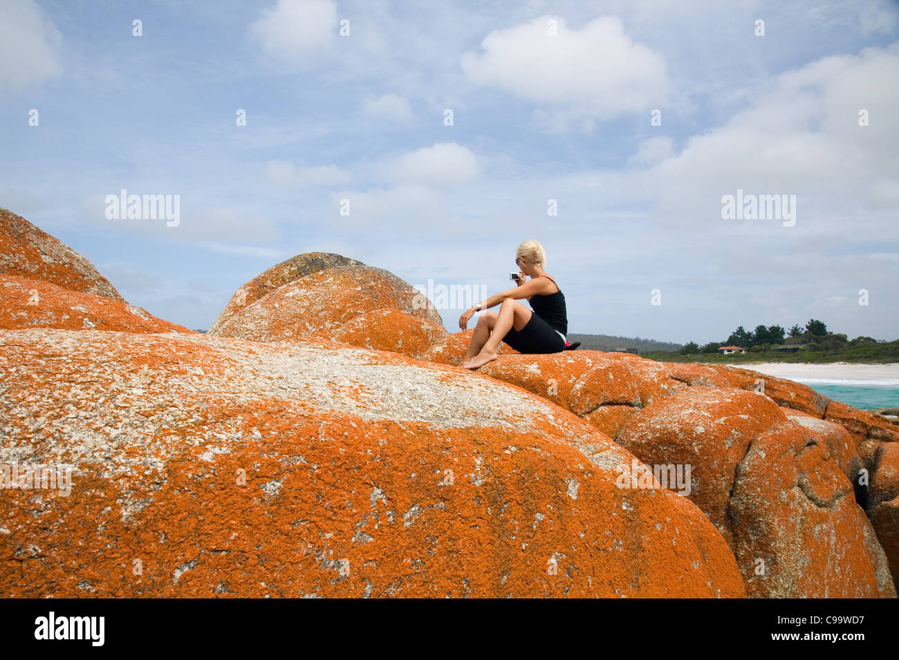 A woman sits atop the orange lichen rocks of Binnalong Bay in the Bay ...