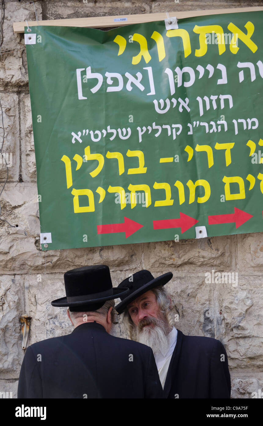 Two orthodox jews talking with poster in hebrew in bkgd. Mea Shearim ...