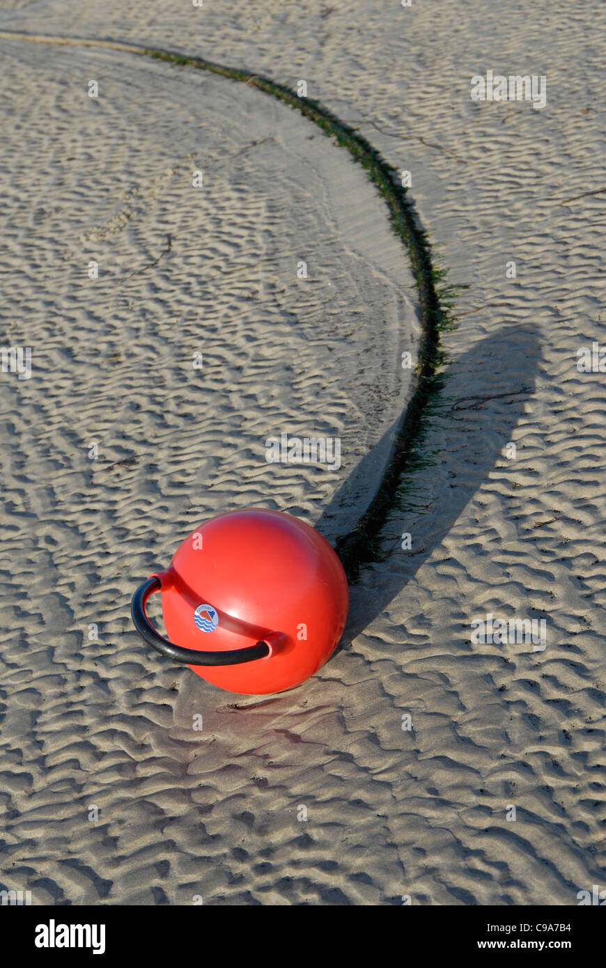 Orange marker buoy and chain lying on rippled sand Stock Photo - Alamy